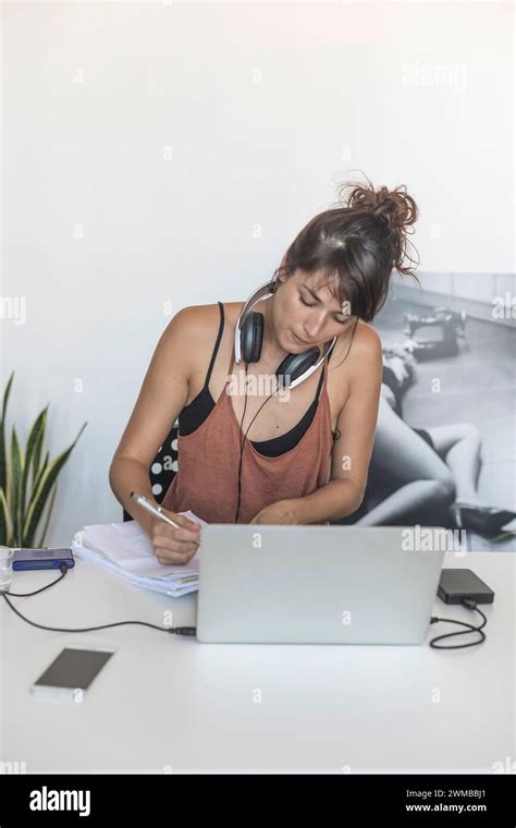 A Dedicated Student Immerses Herself In Study With Her Laptop Papers And Headphones At A Tidy
