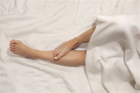 Female Legs With Bare Feet In White Bedding Girl Is Lying In Bed With