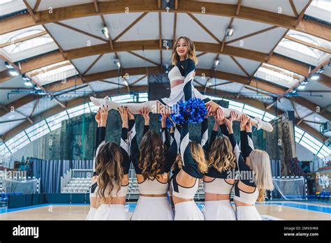 A Cheerleader Doing A Full Split And Smiling At The Camera While Being Held By Her Teammates