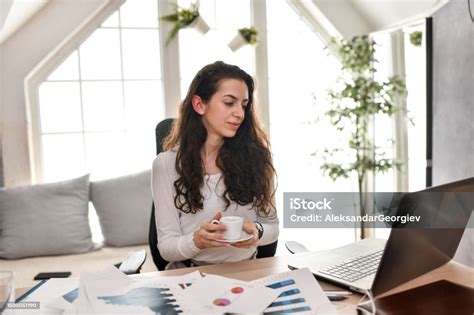 Female Data Analyst Using Graphic Charts In Office While Drinking