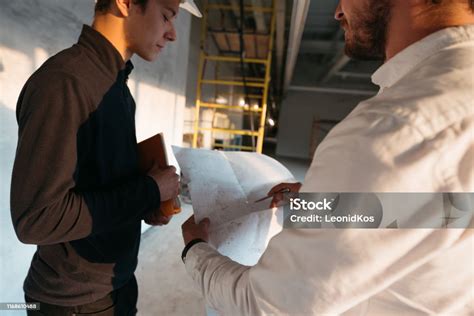 건설 현장에서 건축 작업자 및 건축가가 건설 도면을 논의합니다 안전 하드 햇을 착용한 두 명의 산업 엔지니어가 상업용 건물 구조에 대한 회의를 가졌습니다 2명에 대한 스톡