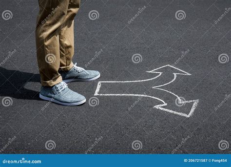 Young Man Standing On A Street With Arrow Signs Pointing In Different