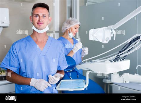 Dentist Standing In Dental Office With Dental Assistant Background