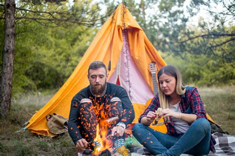 아름 다운 커플 앉아 캠프 파이어 주위에 캠핑 텐트와 배경에 남자 막대기로 화재 제스처 건강한 생활방식에 대한 스톡 사진 및 기타 이미지 Istock