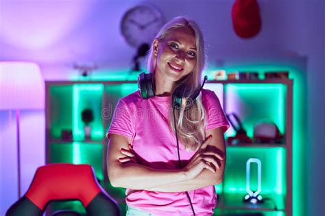 Young Blonde Woman Streamer Wearing Headphones Standing With Arms Crossed Gesture At Gaming Room