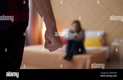 Husband With Clenched Fist Goes To Wife In Fear Sitting On Bed Back