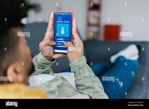 Young Adult Man Using Iot App On Smart Phone Controlling Temperature At
