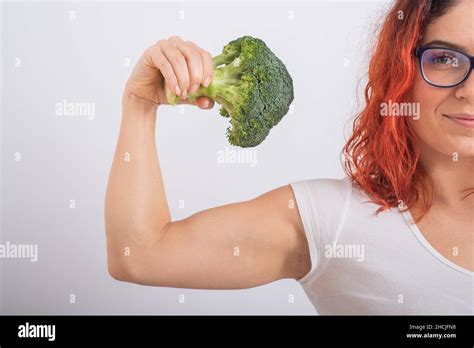 Caucasian Woman Holding Broccoli And Demonstrating Biceps Over White