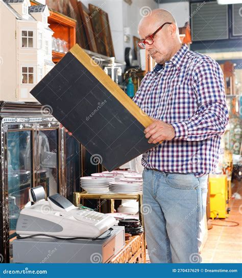 Portrait Of Mature Man Choosing Vintage Goods At Antiques Shop Stock