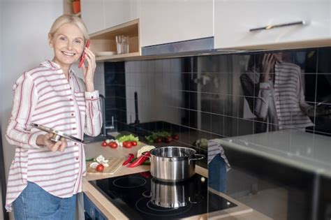 Premium Photo On The Phone Woman Standing Near The Stove In The