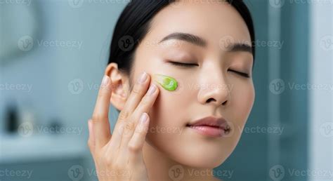 Young Asian Woman Applying Green Facial Serum To Her Cheek For Skincare