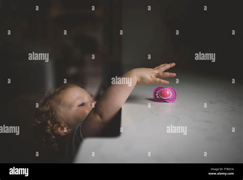 Side View Of Girl Taking Pacifier From Kitchen Counter At Home Stock