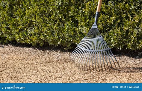 A Rake Laying In The Middle Of Some Gravel Next To Bushes Stock Image