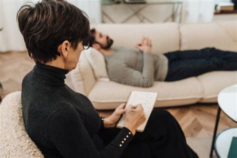 Female Psychologist Writing Down Notes During Therapy Session With Man