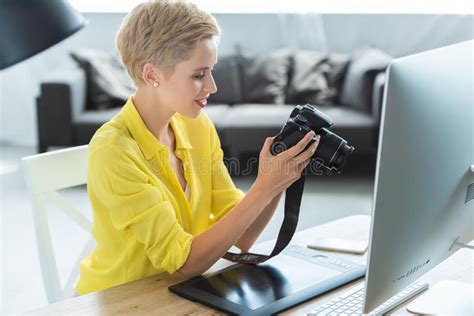 Side View Of Female Photographer Looking At Camera Screen At Table With