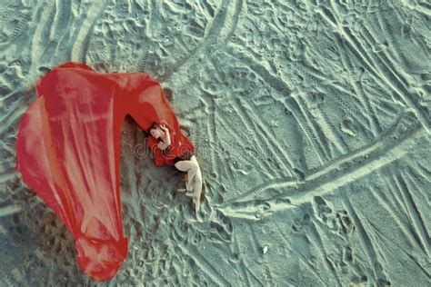 Girl In Black Swimsuit With Fluttering Red Cloth Lies On Sandy Beach