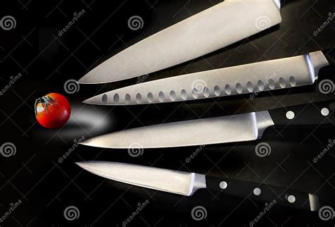 Assorted Sharp And Shiny Kitchen Knives Are Seen With A Small Tomato In