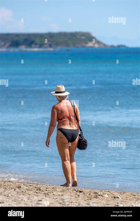 Older Woman Wearing Bikini Walking Along The Waters Edge On The