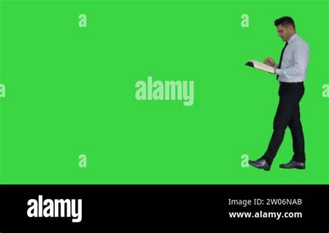 Young Confused Man Trying To Read Smart Book Misunderstanding Content While Walking On A Green