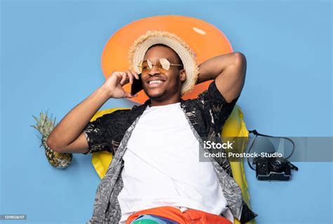 트렌디 한 여름 옷을 입은 펑키 한 흑인 남자 풍선 릴로에 누워 파란색 배경 상단 보기를 통해 스마트 폰에 말하기 남자에 대한