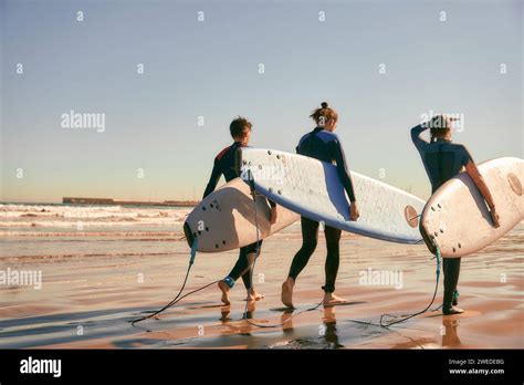 Back View Of Surfers With Surfboards In Wetsuit Are Walking On The
