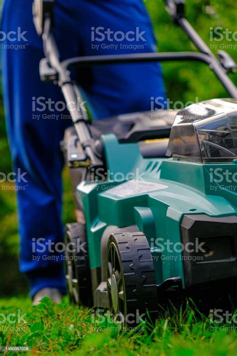 녹색 잔디 깎는 기계 클로즈업은 여름 정원에서 잔디를 깎습니다 정원을위한 기술과 장비 정원에서 여름 작업 한 남자가 정원에서 잔디 깎는 기계로 녹색 육즙이 많은 풀을