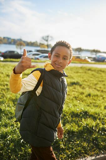 어깨에 배낭을 씌운 흑인 아이의 수직 야외 이미지 도시 거리의 공원에서 훌륭한 사인 워키그로 자신의 기분에 대한 Qestion에 대한 엄지 손가락 대답 스포츠 클럽에서