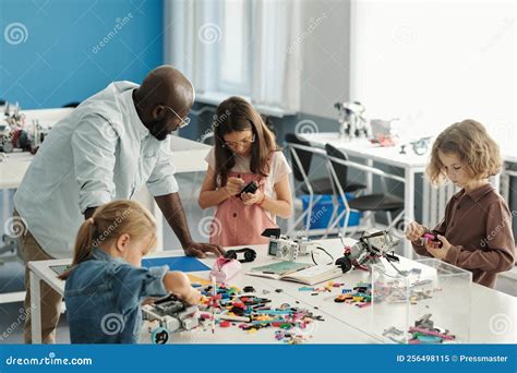 Group Of Youthful Learners Constructing Robots At Lesson With Teacher