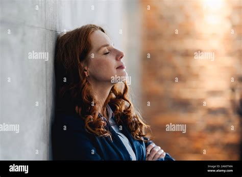 Redheaded Businesswoman Having A Break Leaning Against A Wall In Office
