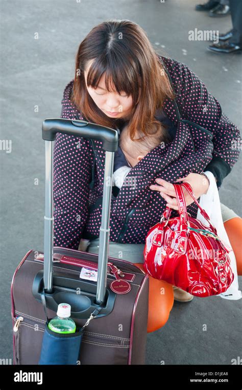 Japanese Woman With A Baby Tucked Inside Her Robe Bends Down To Adjust Her Suitcase On A
