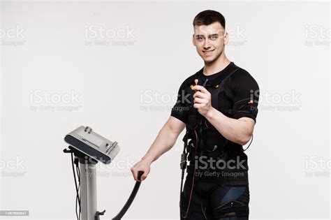 Ems를 입은 근육질의 남성 운동선수는 흰색 배경에 근육을 자극하기 위해 전기 충격을 사용하는 접촉기를 손에 들고 있다 전기 근육 자극 슈트에서 스포츠 훈련 20 24세에