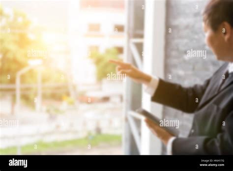 Businessman Holding Tablet And Pointing His Finger Out Of Window Blur For Use As Background