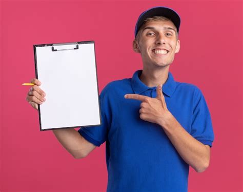 Il Giovane Ragazzo Delle Consegne Biondo Sorridente Tiene E Indica Gli