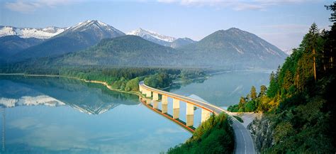 Reflections Of A Road Bridge Over Lake Sylvenstein With Mountains In