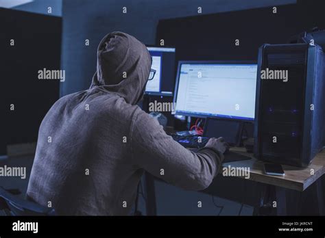 computer hacker wearing hooded shirt using computer at table stock