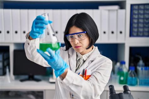 Young Chinese Woman Scientist Holding Measuring Liquid At Laboratory