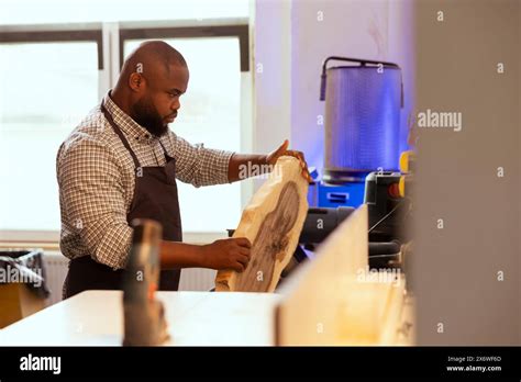 African American Carpenter In Woodworking Shop Inspecting Wood Before