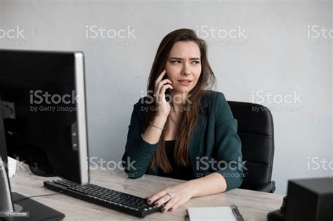 흰색 사무실에서 컴퓨터 화면에 대해 전화를 말하는 젊은 비즈니스 여성의 초상화 여성 기업가 가 전화 하 고 테이블에 앉아 컴퓨터와 함께 작업 전화 작업 전화 기업 비즈니스에