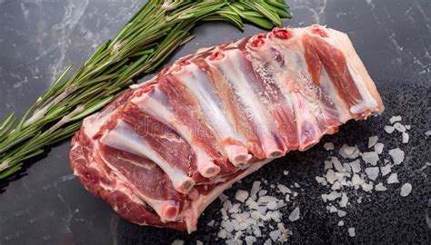 Macro Photo Of Sliced Lamb Carcass On Black Marble With Sea Salt Crumbs And Rosemary Sprig Stock