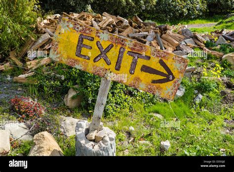 An Exit Sign Pointing Down Toward The Ground Hand Painted In Yellow Orange And Brown With