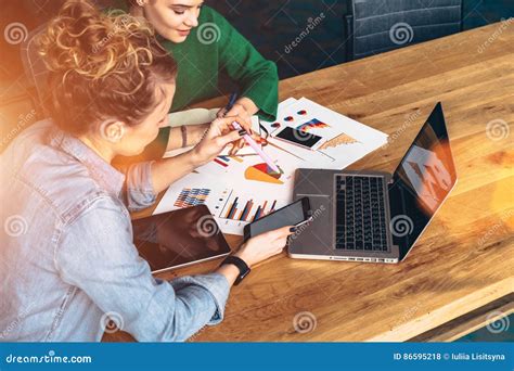 Two Young Business Women Sitting At Table In Front Of Laptopon Table