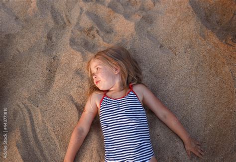 Little Cute Girl In A Striped Swimsuit Lies On A Sandy Beach Stock