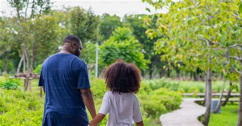 공원에서 행복한 혼혈 가족 어린 딸이 손을 잡고 정원에서 함께 걷고 있는 아프리카 아버지 아빠와 아이 여자 아이는 여름 야외