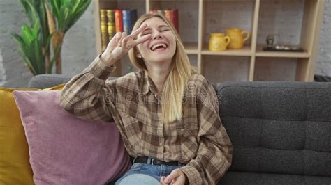 Joyful Young Blonde Striking A Victory Pose On Her Apartment Sofa