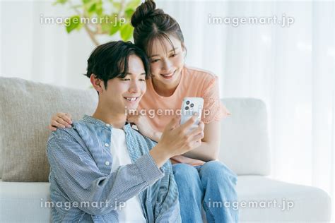 リビングでくつろぎながらスマホを見る日本人の若いカップル （男女 人物）の写真素材 [252001085] イメージマート