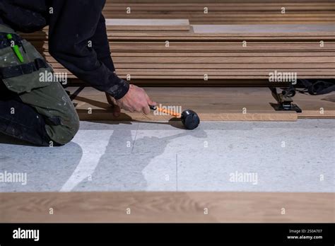 An Individual Uses A Rubber Mallet To Position Wooden Floorboards