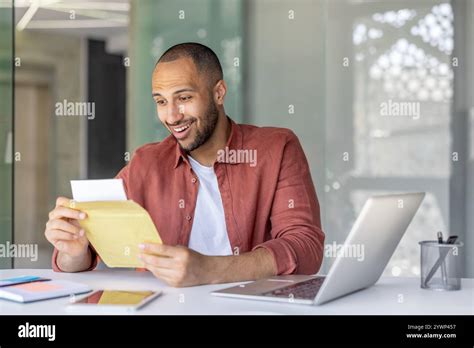 A Cheerful Man Opening And Reading An Envelope At His Office Desk He