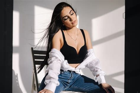 Premium Photo Sexy Woman In Black Topic And Blue Jeans Sits On Chair