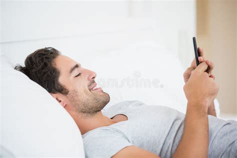 Young Man Smiling While Using Mobile Phone On Bed Stock Image Image