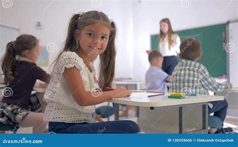 Portrait Of Lovely Learner Girl At Desk During Education Lesson In